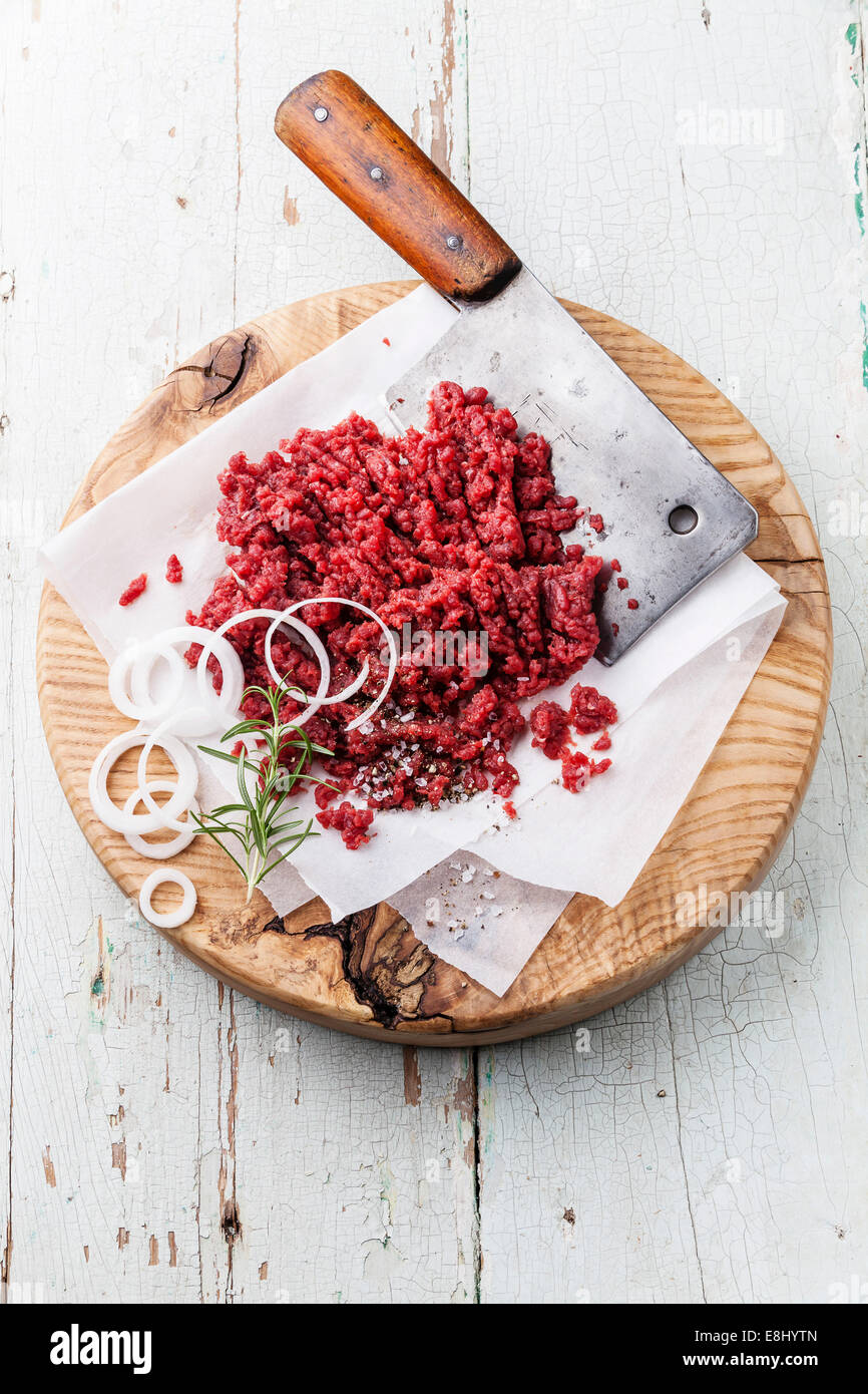 Raw chopped meat and meat cleaver on wooden cutting board on blue ...