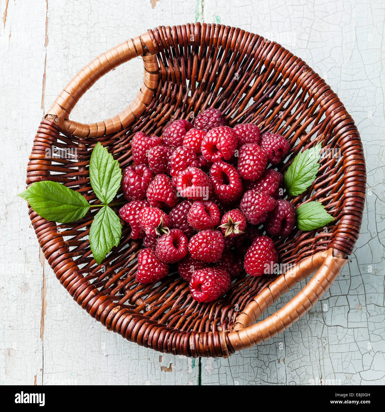Raspberries with leaves in basket on blue background Stock Photo - Alamy