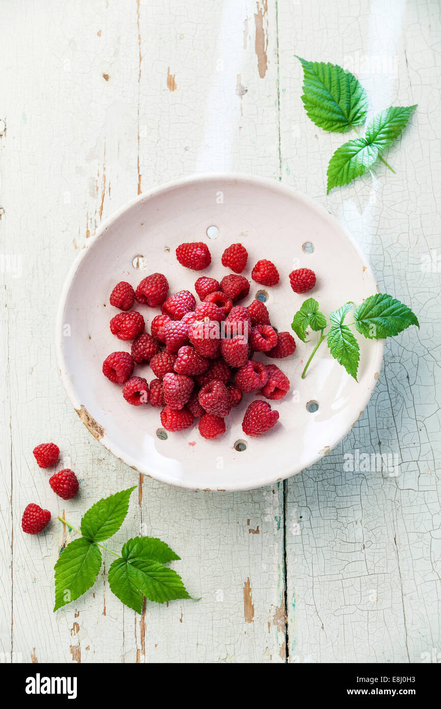 Raspberries with leaves in vintage ceramic colander on blue wooden ...