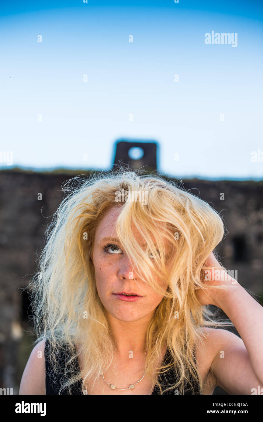 A wild-haired unkempt crazy feral deranged blond woman girl in a gritty ...