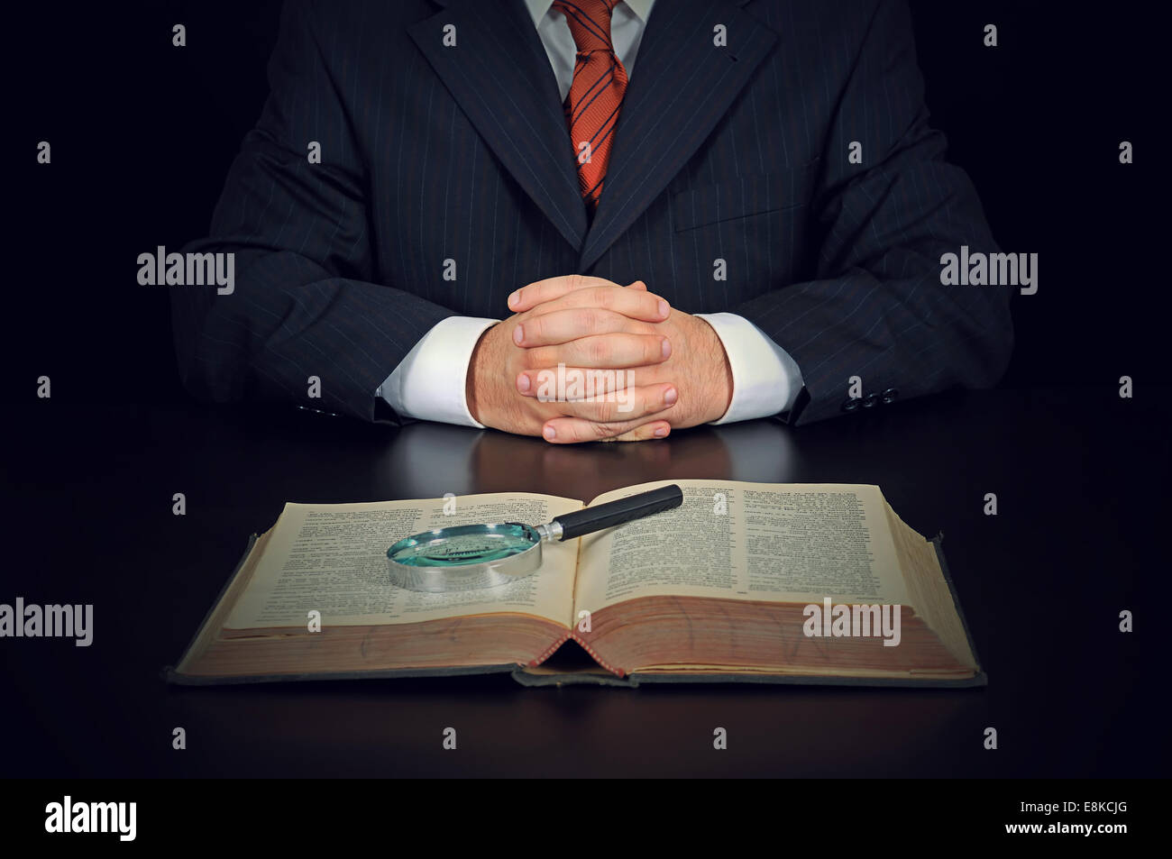 Businessman with old book and magnifying glass on the black background ...