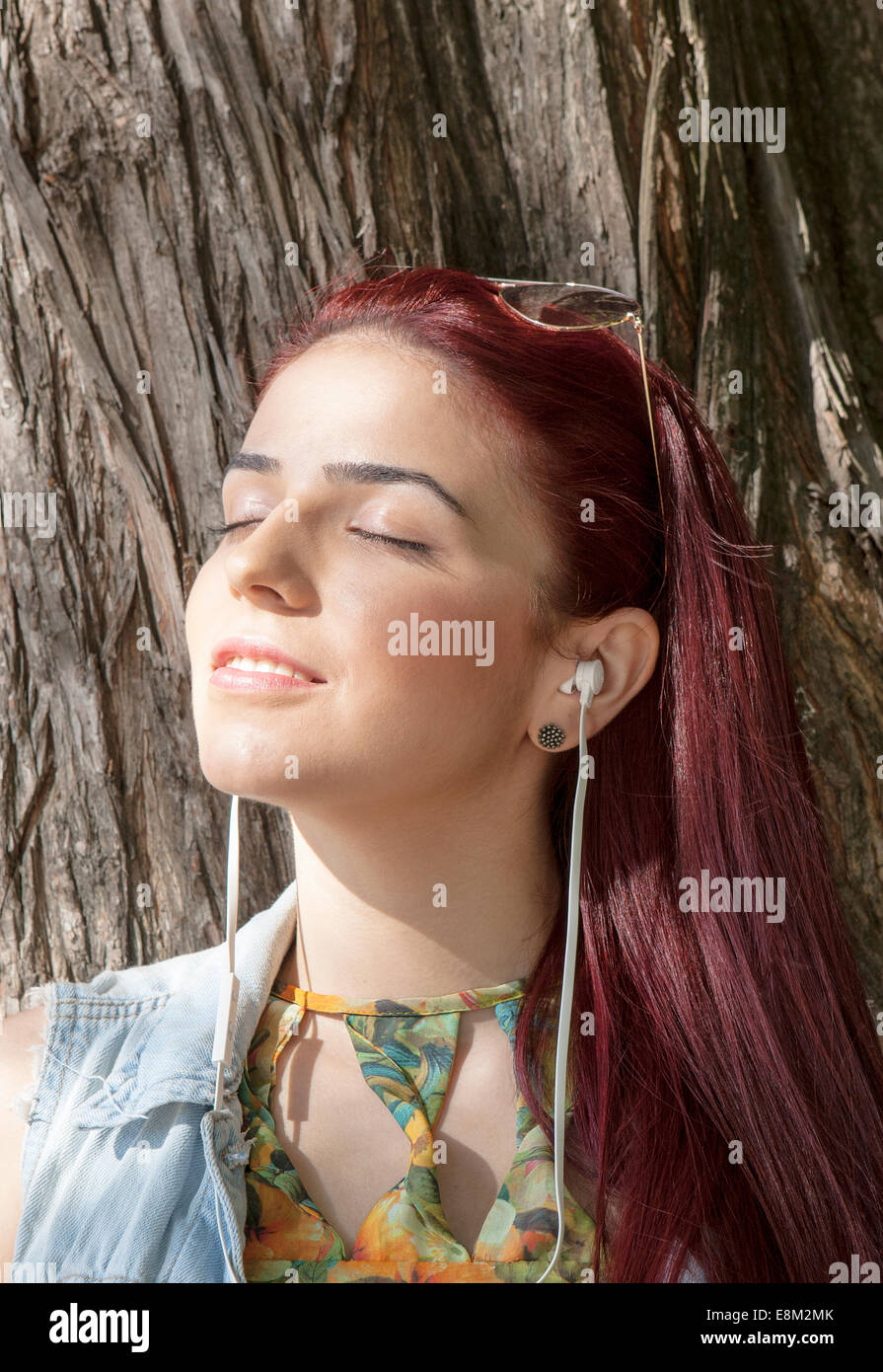 Beautiful young lady leaning on a tree listening music Stock Photo - Alamy