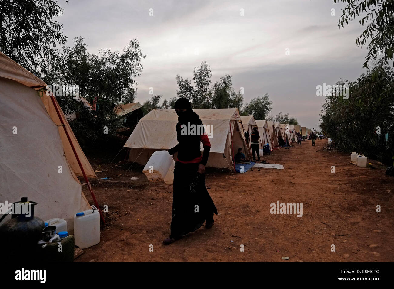 A Yazidi woman walking amid temporary shelter tents at a refugee camp ...