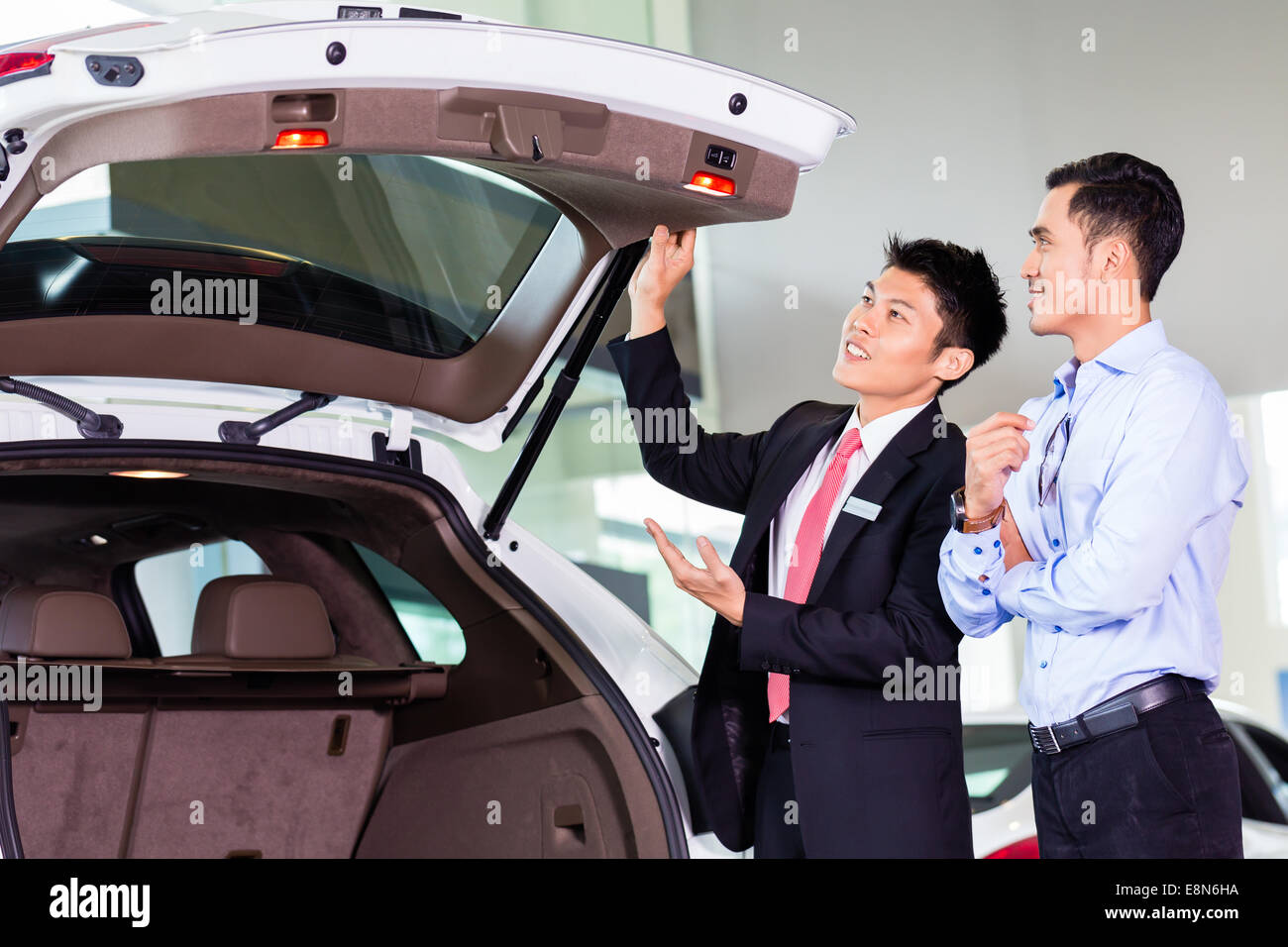 Car salesman in Asian dealership showing trunk of SUV car to customer ...