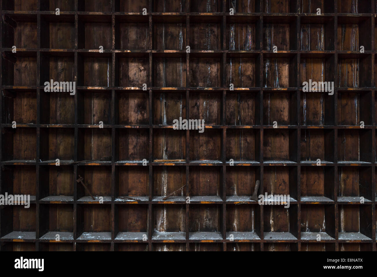 Wide view of an old and distressed, dark wood shelf. Square boxes with ...