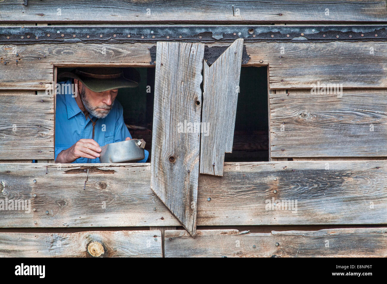 cowboy cooking or eating in an old shack, a face visible through window ...