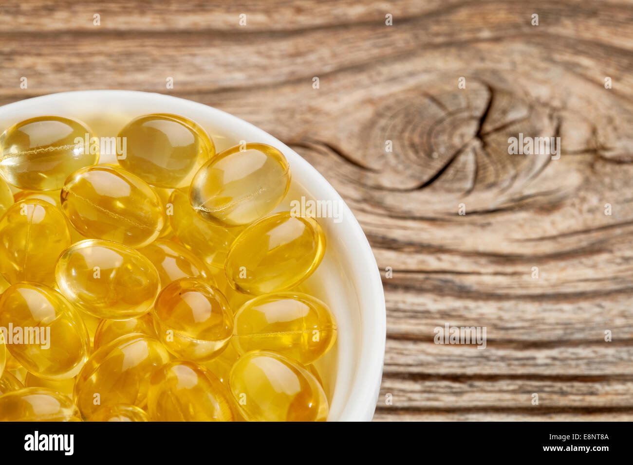 fish oil supplement capsules - a small ceramic bowl on a grained wood ...