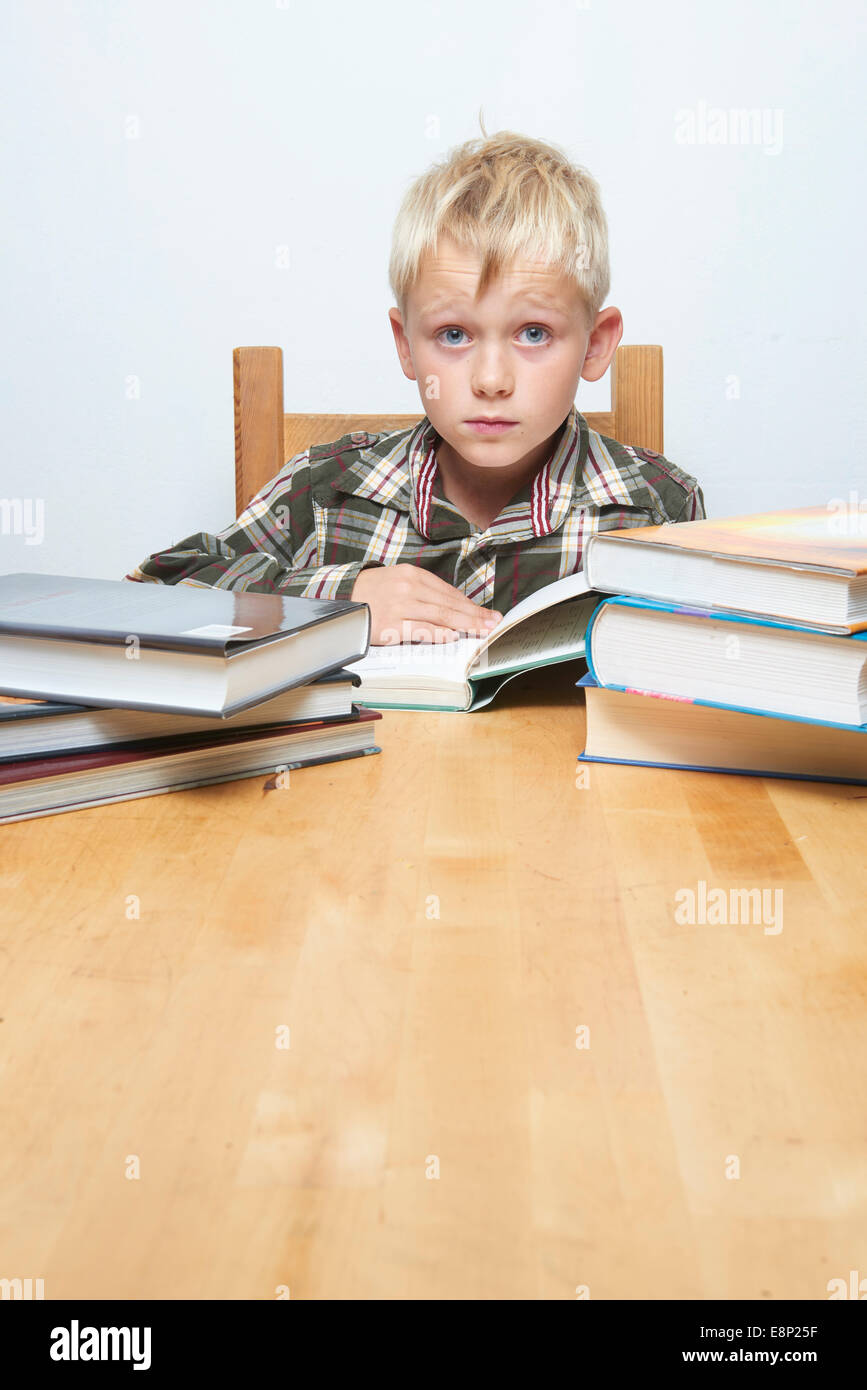 Little child blond focused student boy sitting at desk and reading book ...