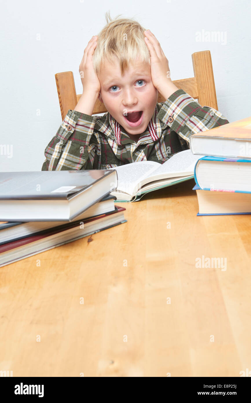 Little child blond focused student boy sitting at desk and reading book ...
