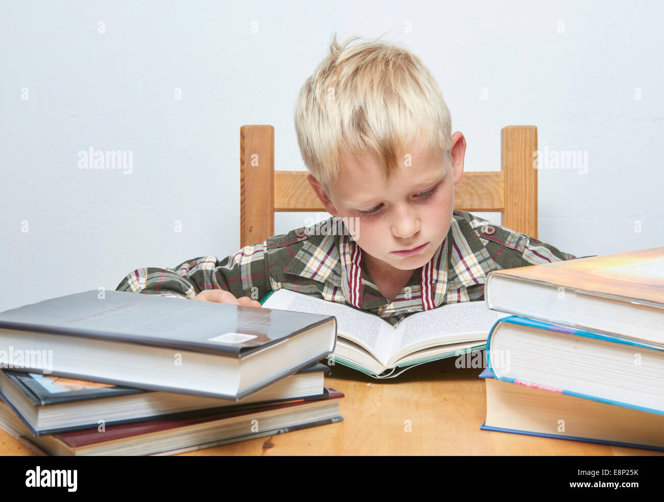 Little child blond focused student boy sitting at desk and reading book ...