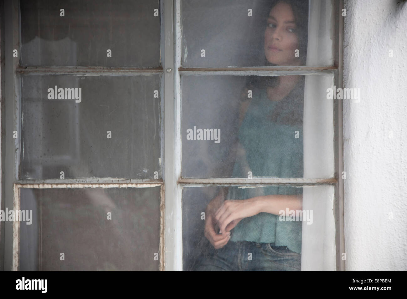 Portrait of young woman looking through window Stock Photo - Alamy