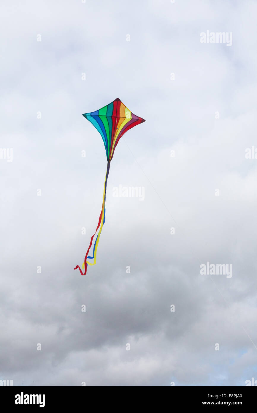Rainbow coloured kite flying against a cloudy sky, West Sussex, England ...