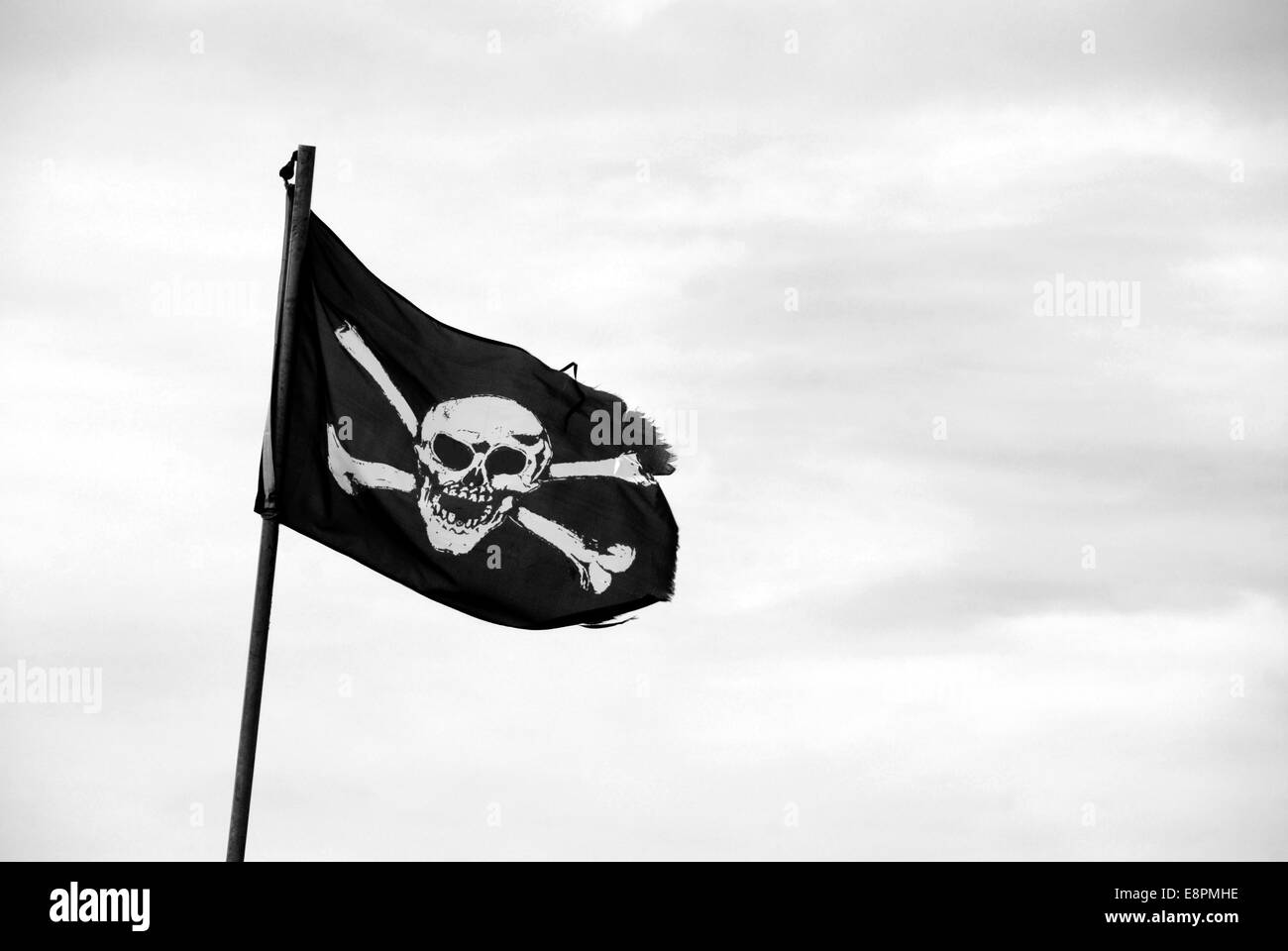Ragged pirate flag with skull and crossbones flying from flagpole ...