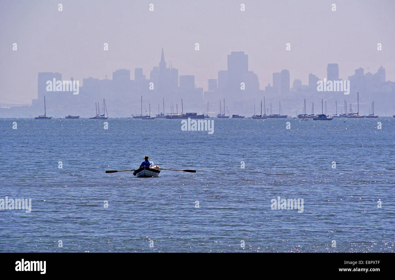 man in rowboat rows on San Francisco Bay with city skyline in the ...
