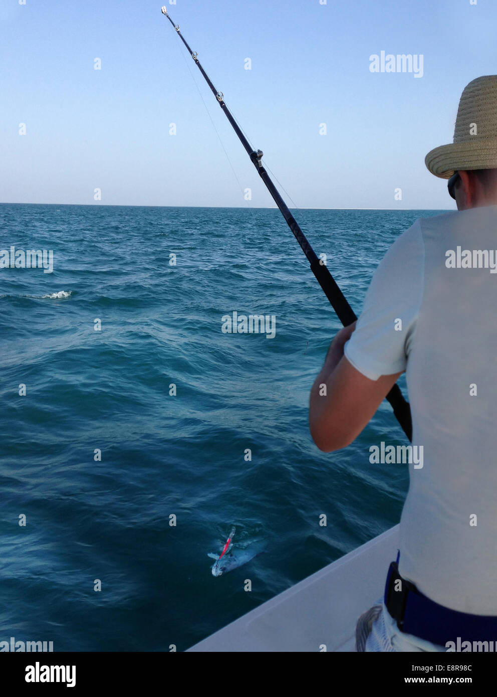 Young man fishing on a ocean. Catching big Queen fish Stock Photo - Alamy