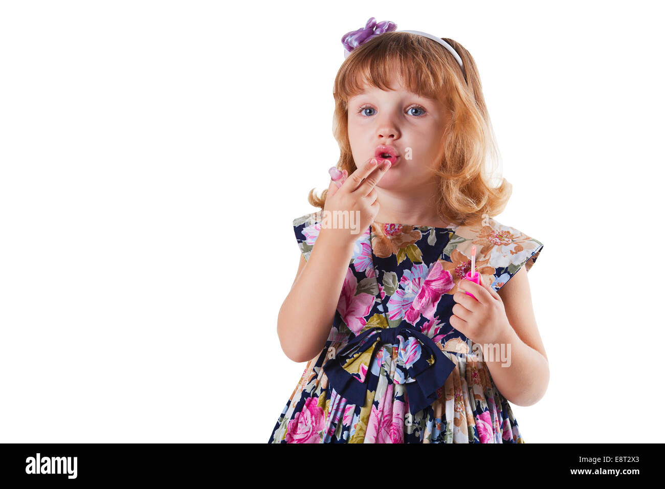 Little girl with lipstick in hand; she is touching her lips, she stands ...