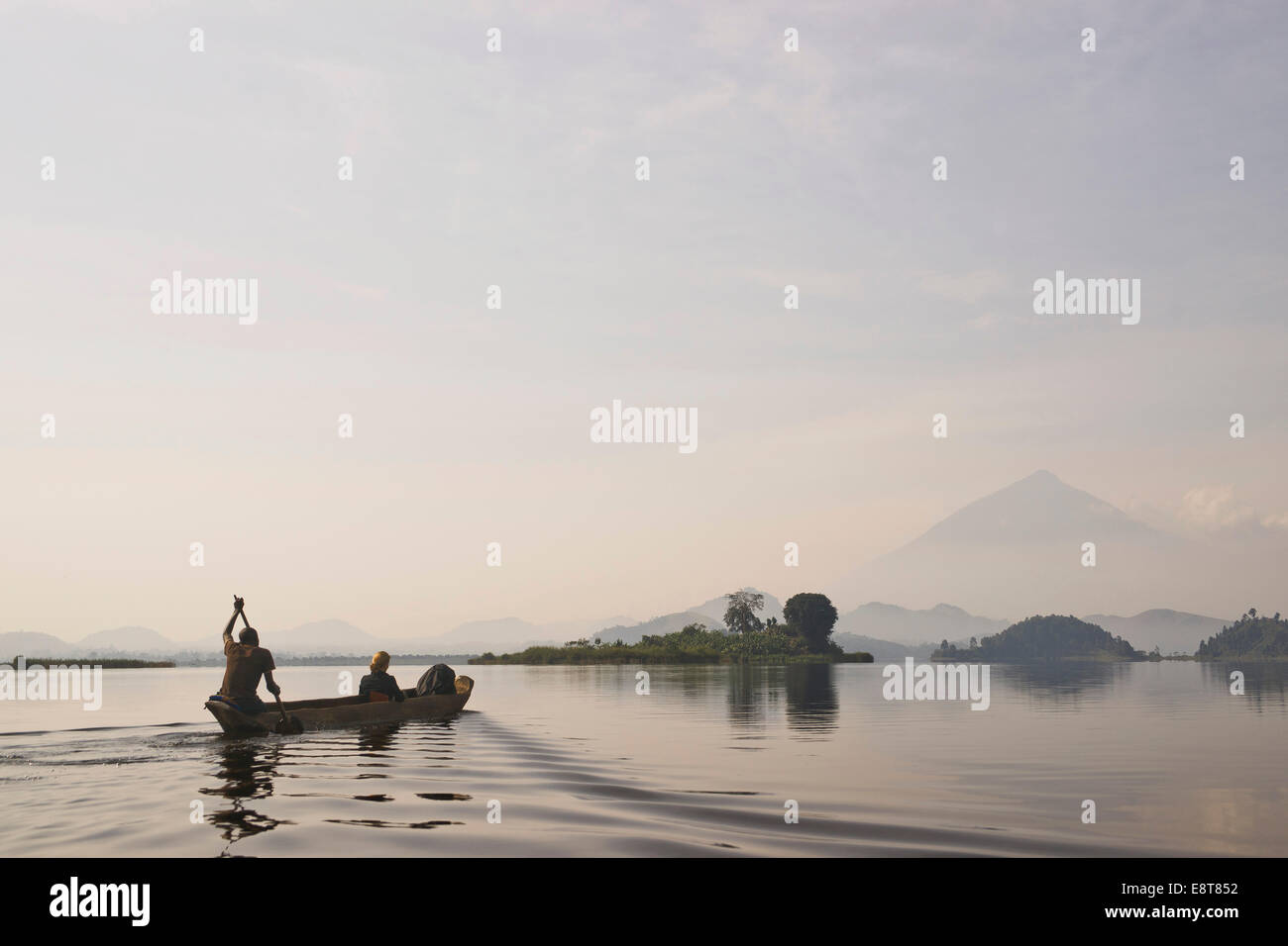 Guide and woman in canoe in the morning mist by Mutanda Lake volcano in ...