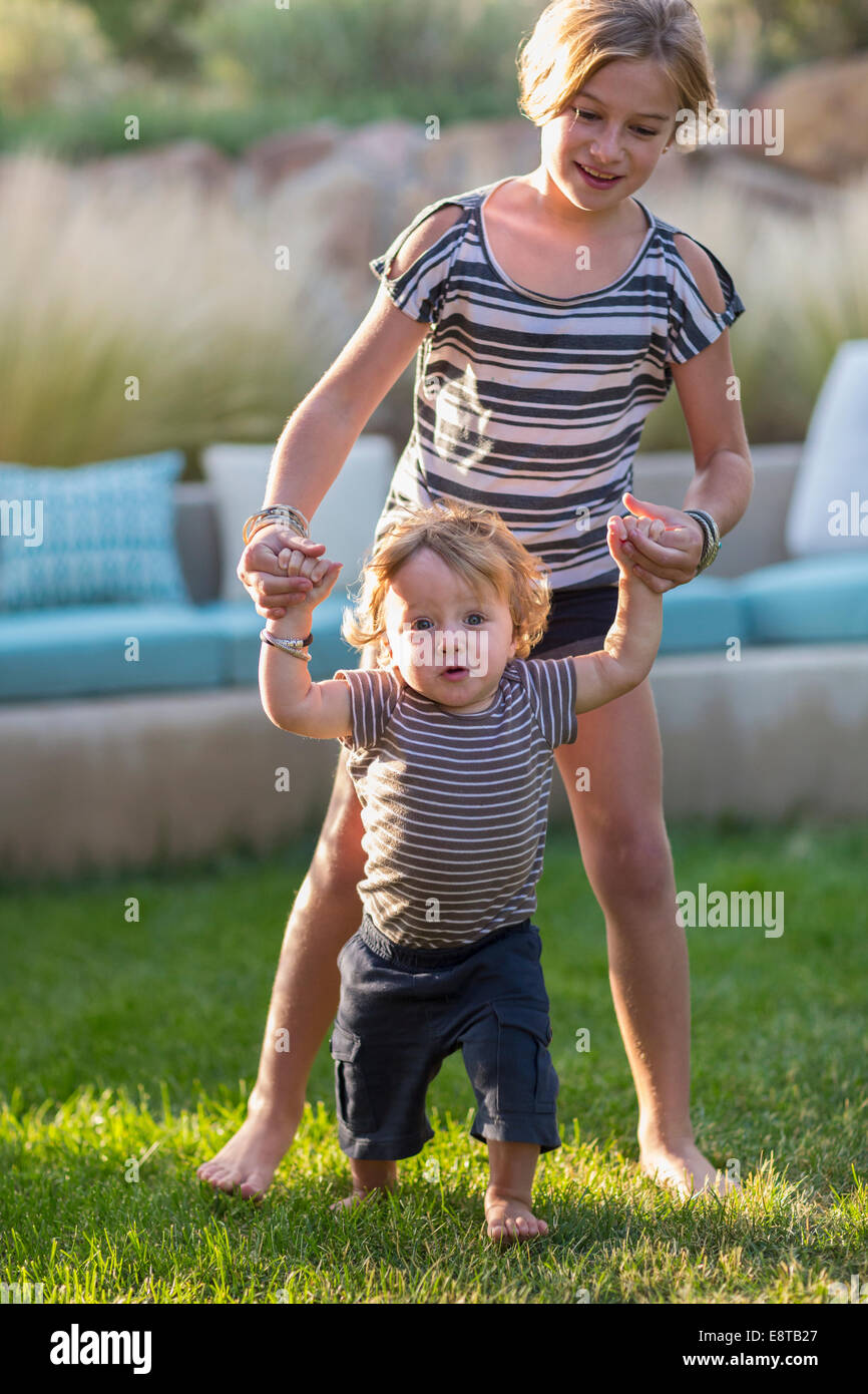 Caucasian sister helping baby brother walk in backyard Stock Photo - Alamy