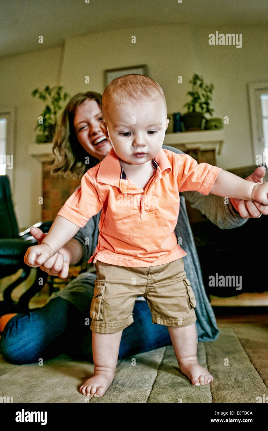 Caucasian mother helping baby walk on living room floor Stock Photo - Alamy