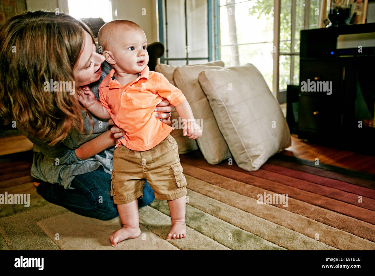 Caucasian mother helping baby walk on living room floor Stock Photo - Alamy