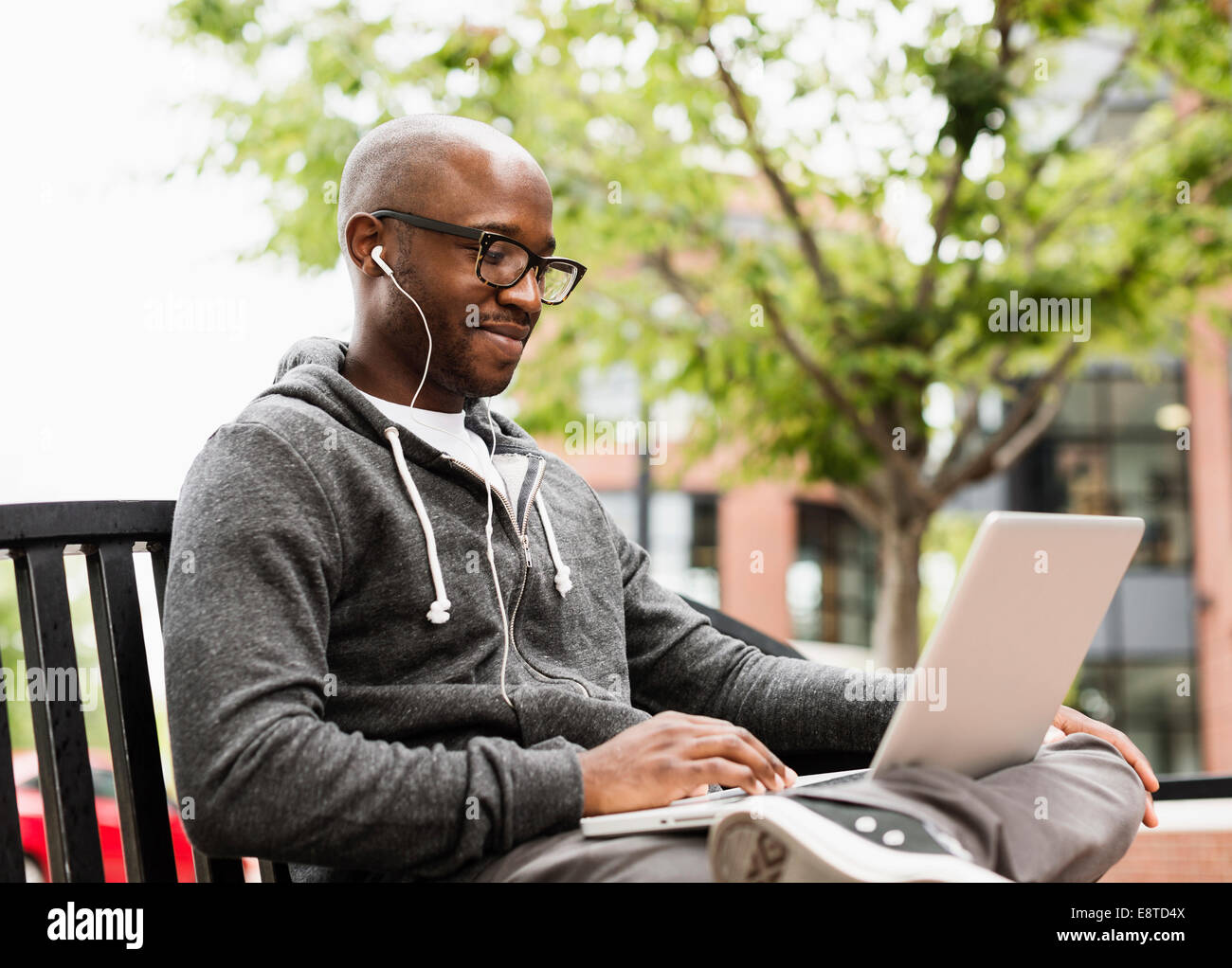 Black man using laptop and earphones on city bench Stock Photo - Alamy