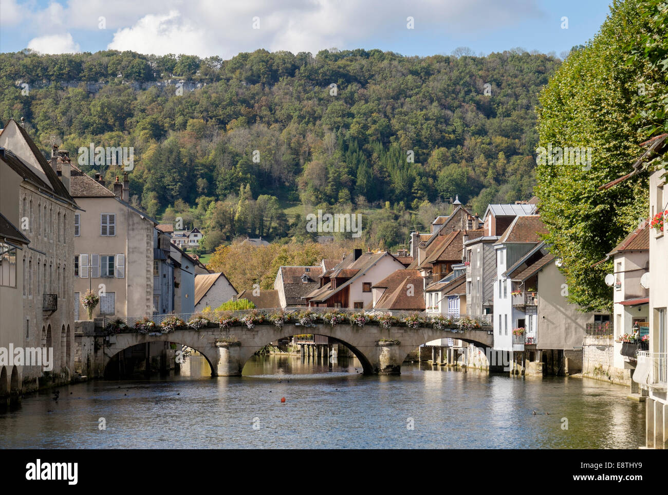 View along River Loue to bridge in town below limestone escarpment ...