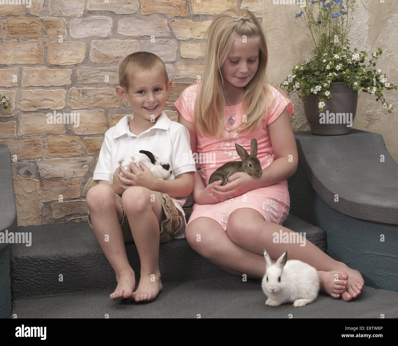 two children sitting on a step holding bunnies. One bunny is at the ...