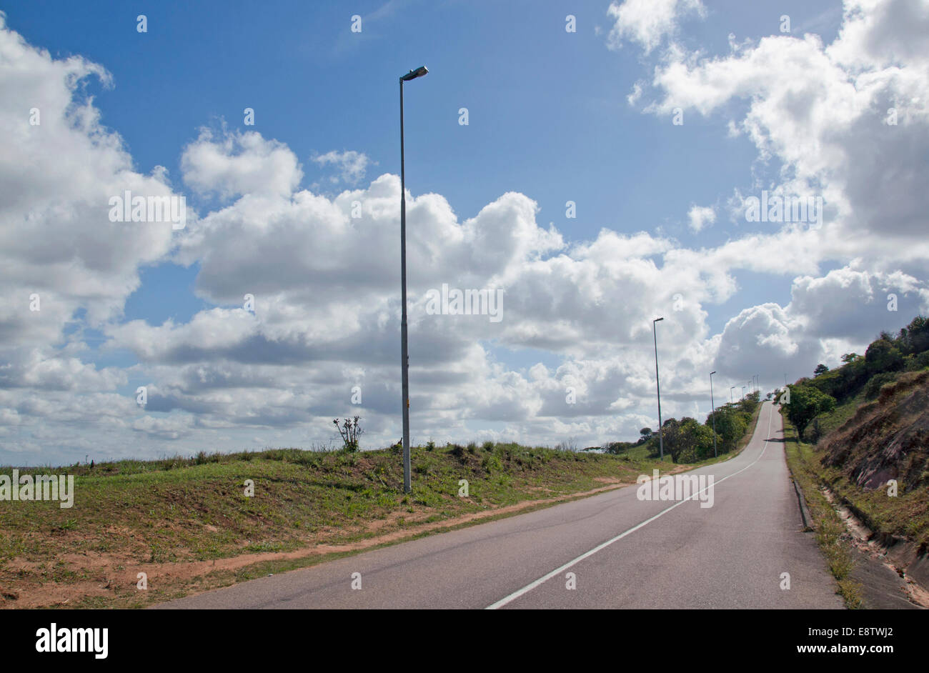 Long straight tarmac road lined with street lamps under cloudy sky ...