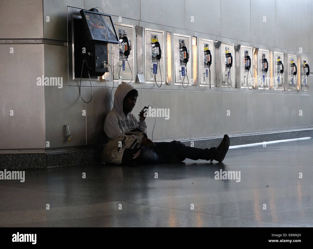 A man in a hooded sweatshirt sits on the ground and types on his ...