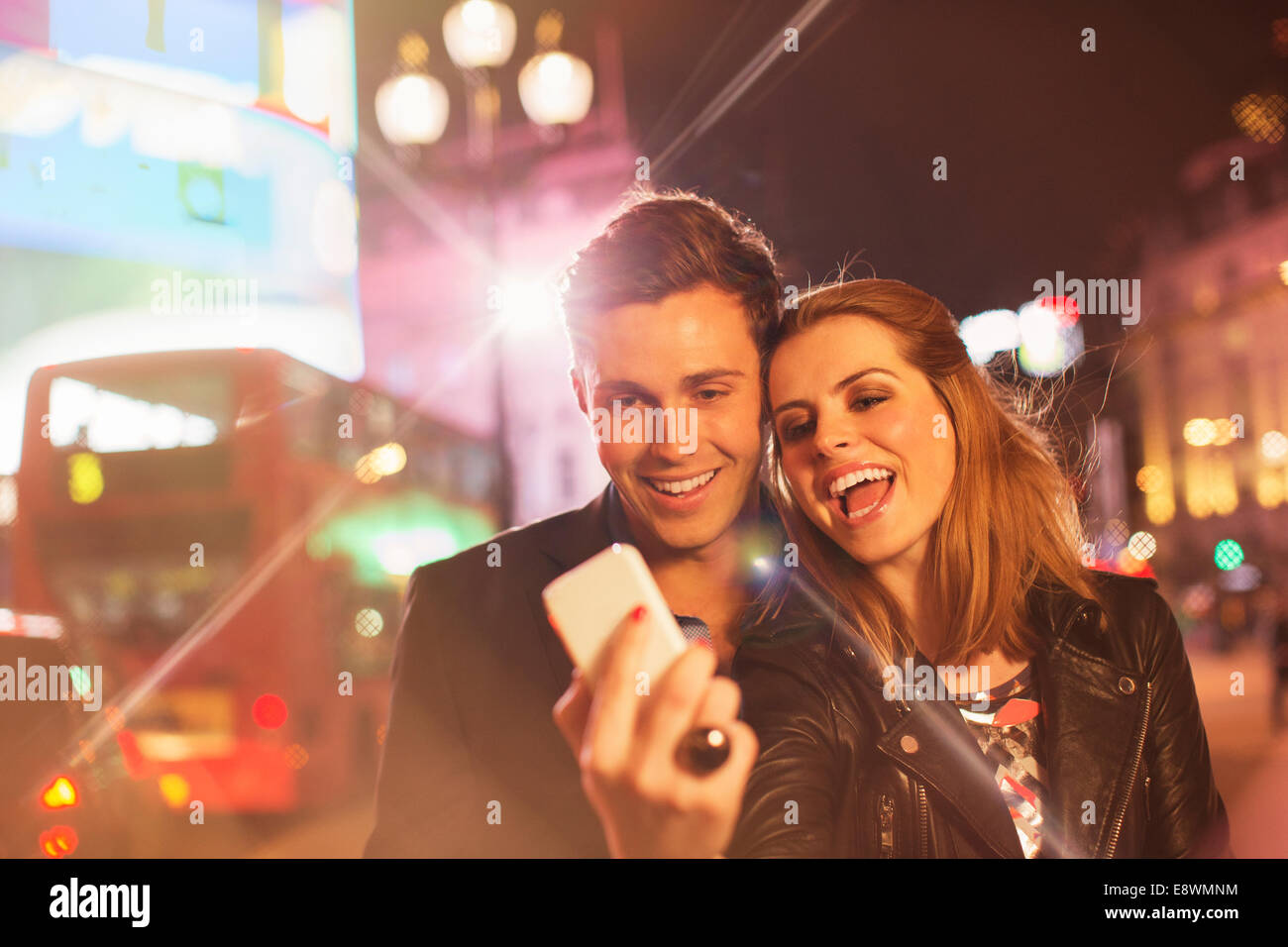 Couple taking cell phone picture together on city street at night Stock ...