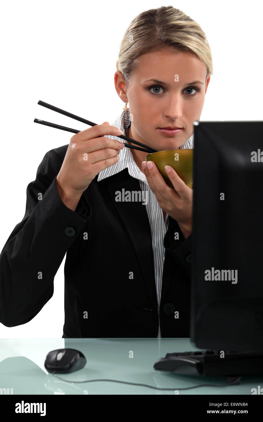 Woman sitting at her computer eating with chopsticks Stock Photo - Alamy