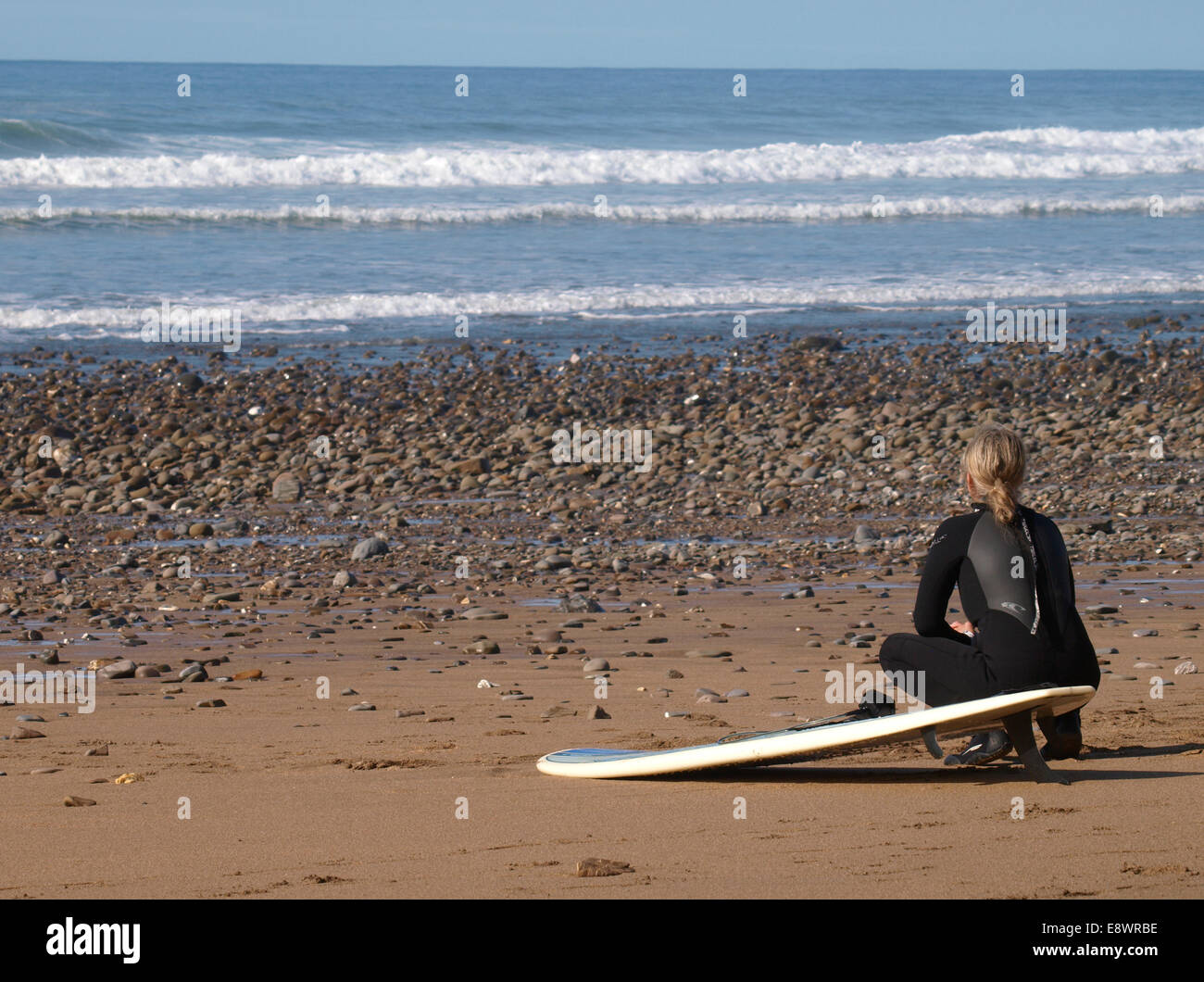 Surfer crouched on the beach watching the waves, Widemouth Bay, Bude ...