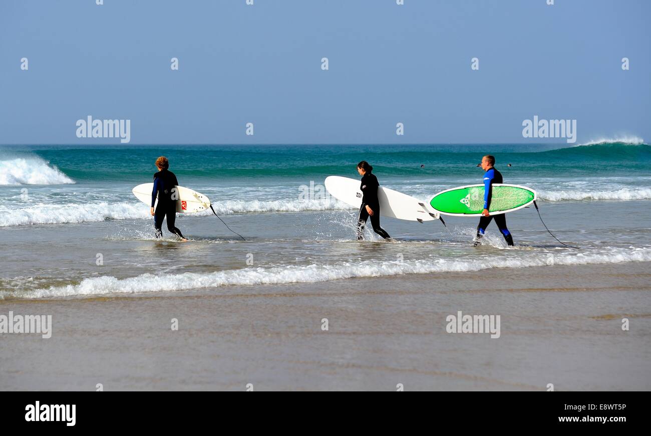 3 three surfers walking into the sea carrying their surf boards ...