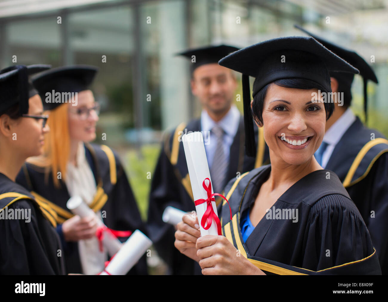 Student in cap and gown smiling with colleges Stock Photo - Alamy