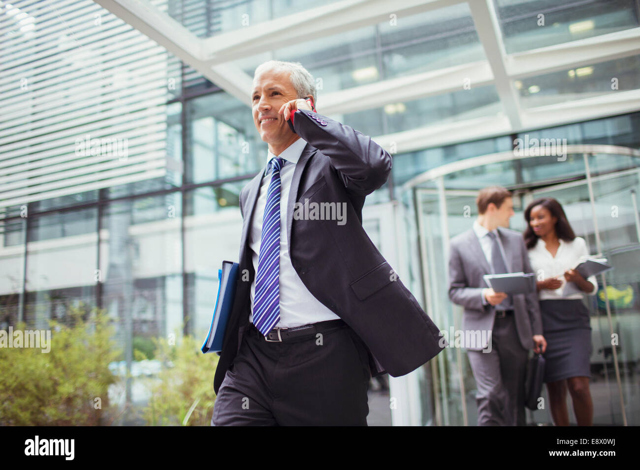 Businessman talking on phone while walking out of office building Stock ...