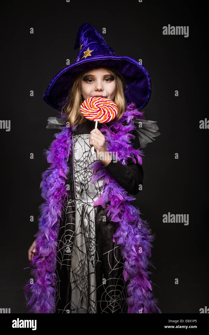 Little beautiful girl with halloween witch costume eat colored candy ...