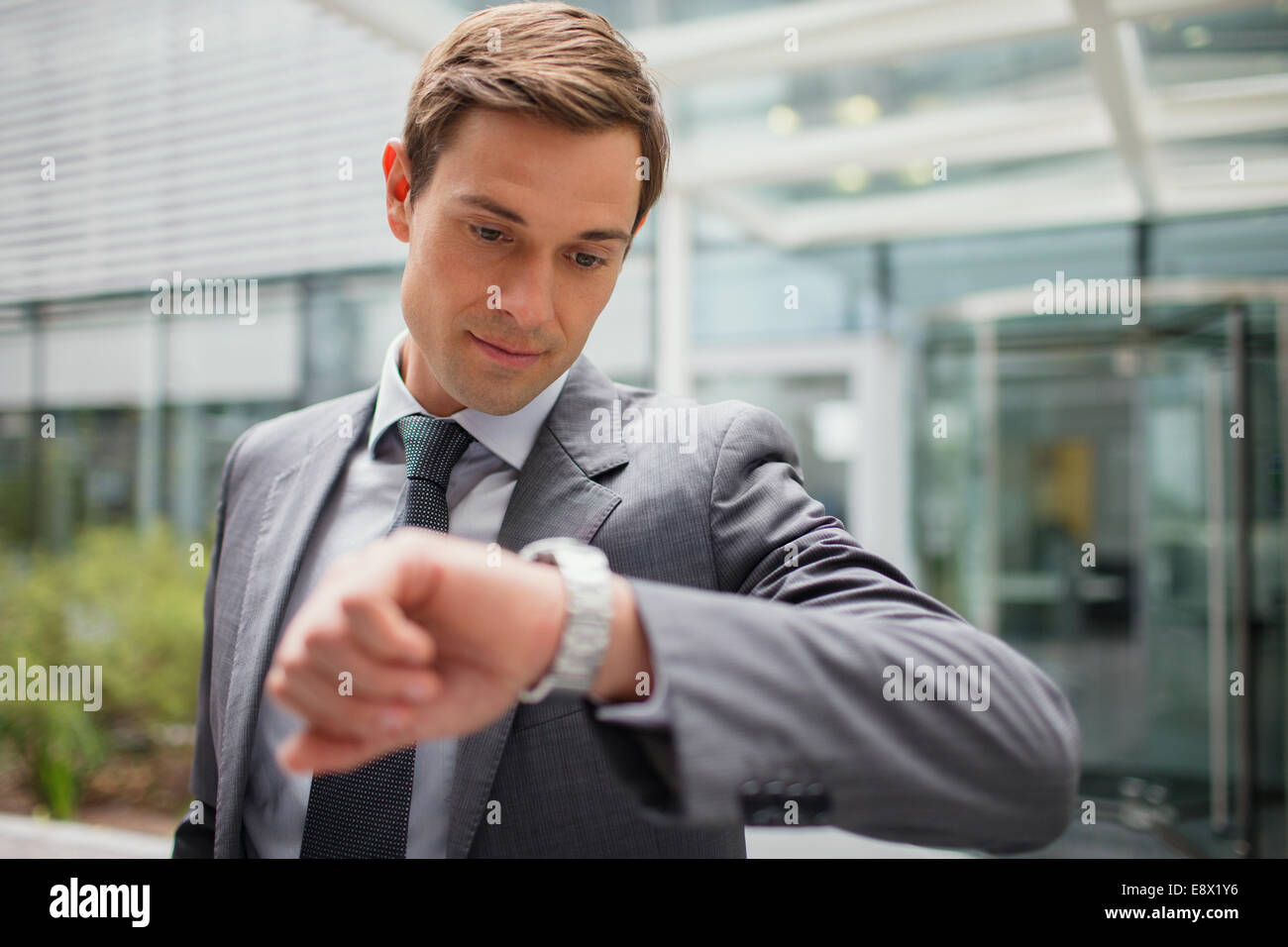 Businessman looking at watch outside office building Stock Photo - Alamy