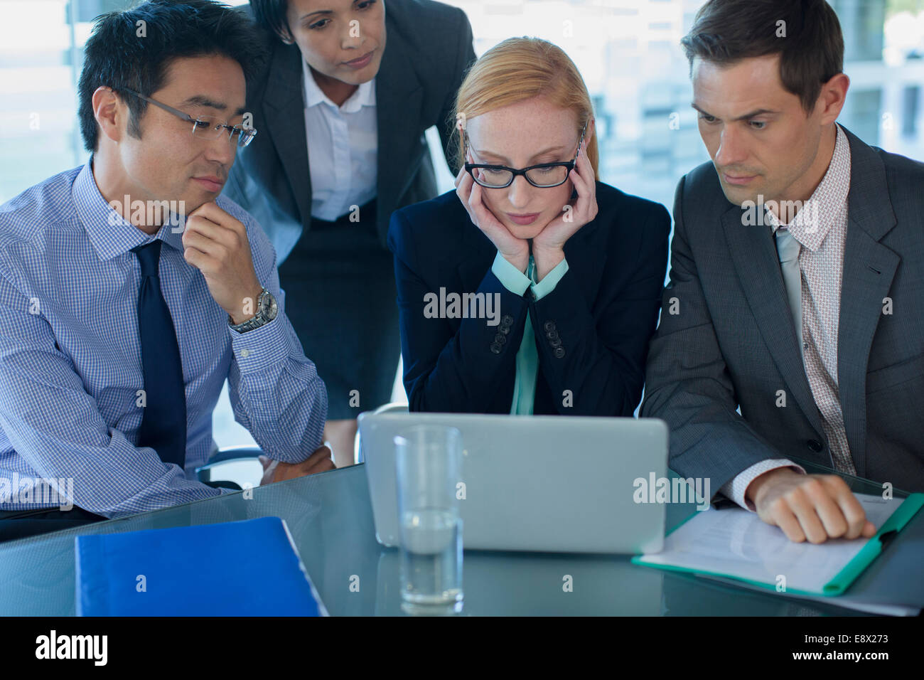 Business people gathered around laptop at table in office building ...