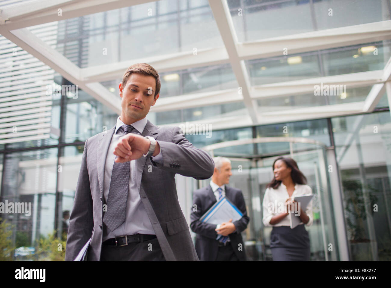 Businessman looking at watch walking out of office building Stock Photo ...