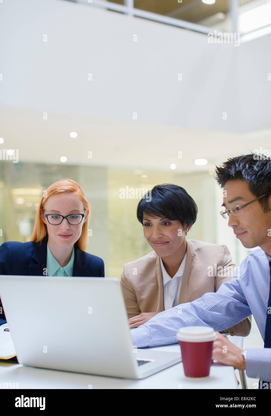 Business people gathered around laptop in office building cafe Stock ...