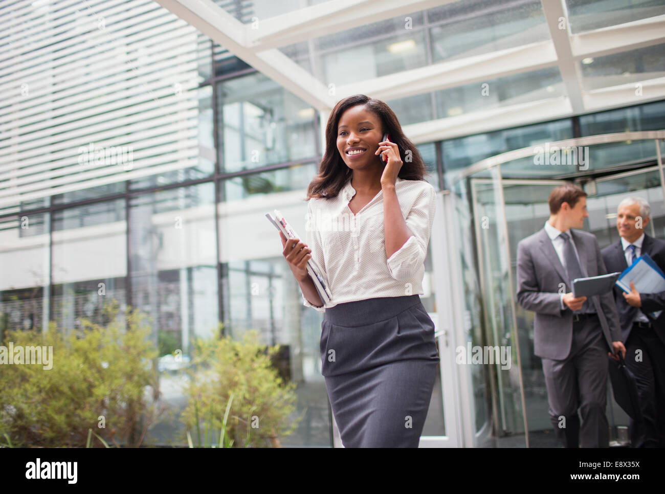 Businesswoman talking on cell phone walking out of office building ...