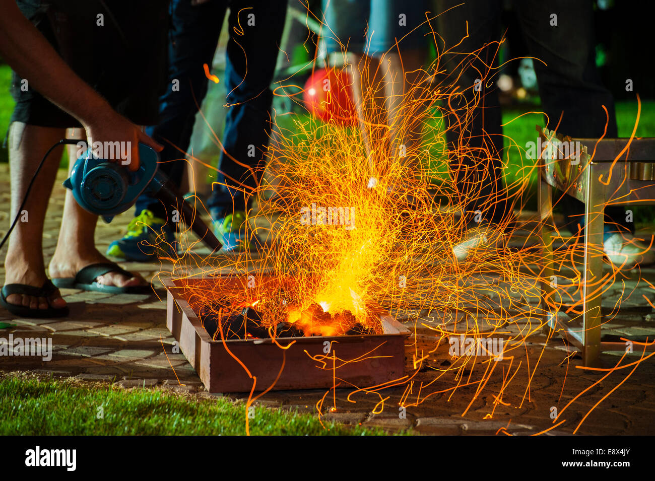 Small BBQ on fire with burning charcoal and flying sparks while people ...