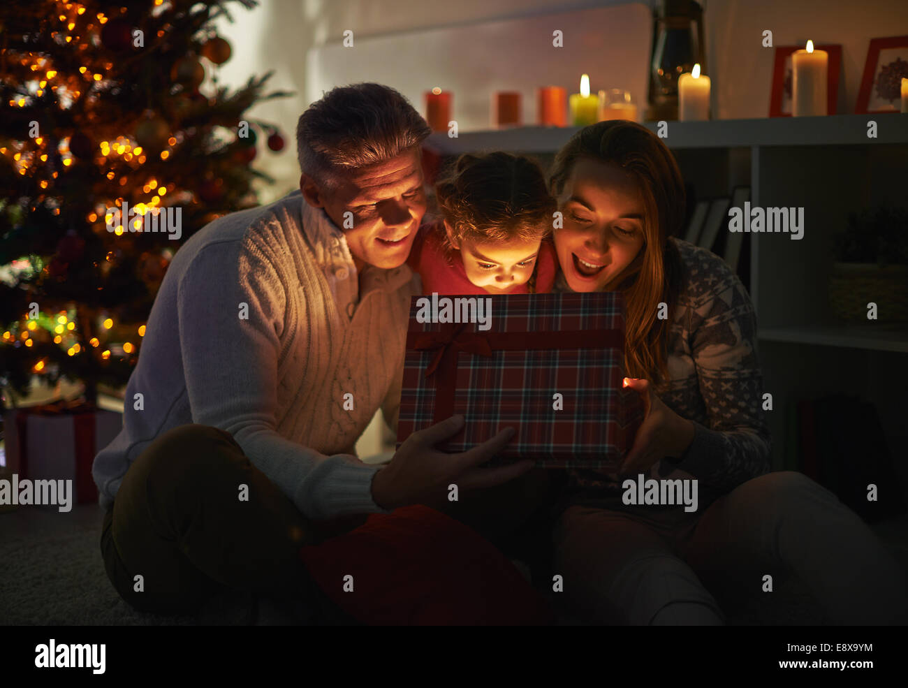 Happy family of three looking into open giftbox on Christmas night ...
