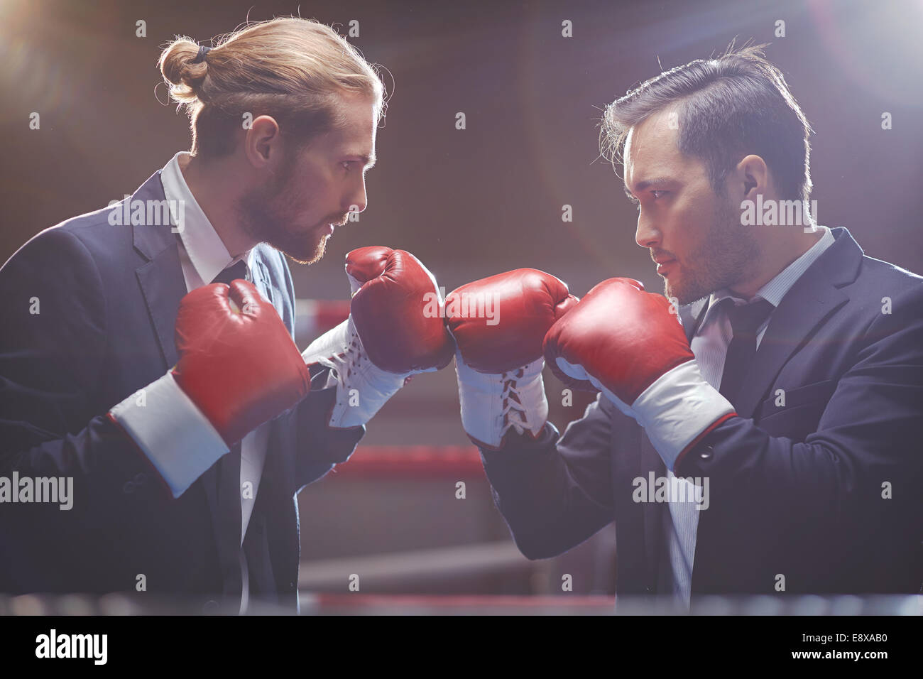 Two competitive businessmen in suits and boxing gloves attacking one ...