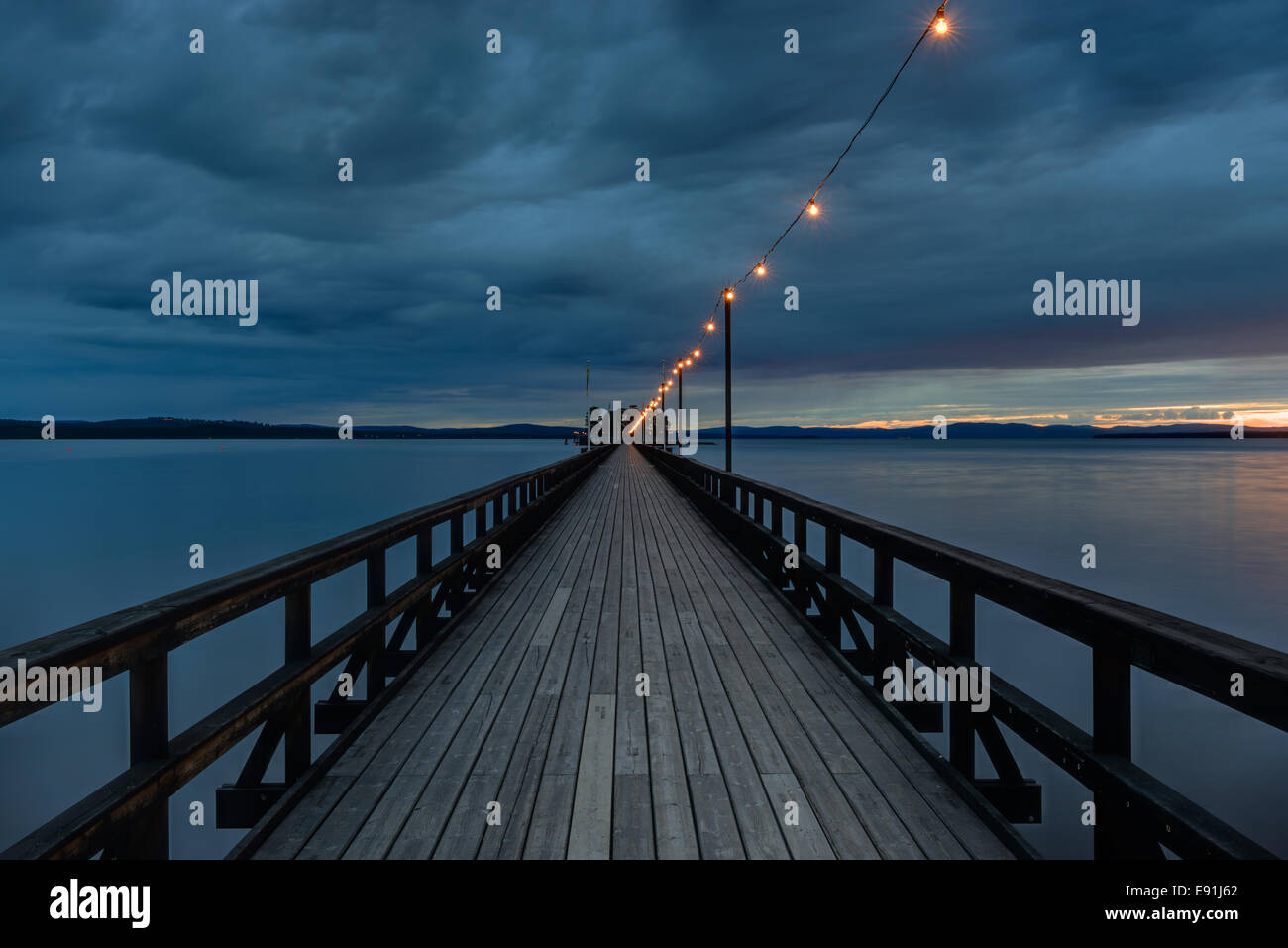 Long wooden pier over a river at night with lights strung overhead ...