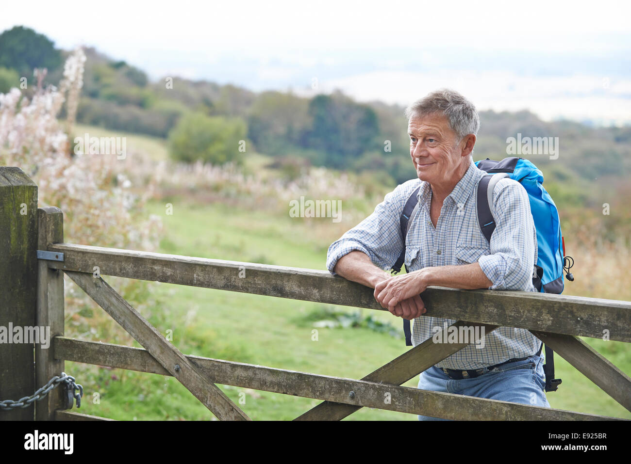 Senior Man Hiking In Countryside Resting By Gate Stock Photo - Alamy