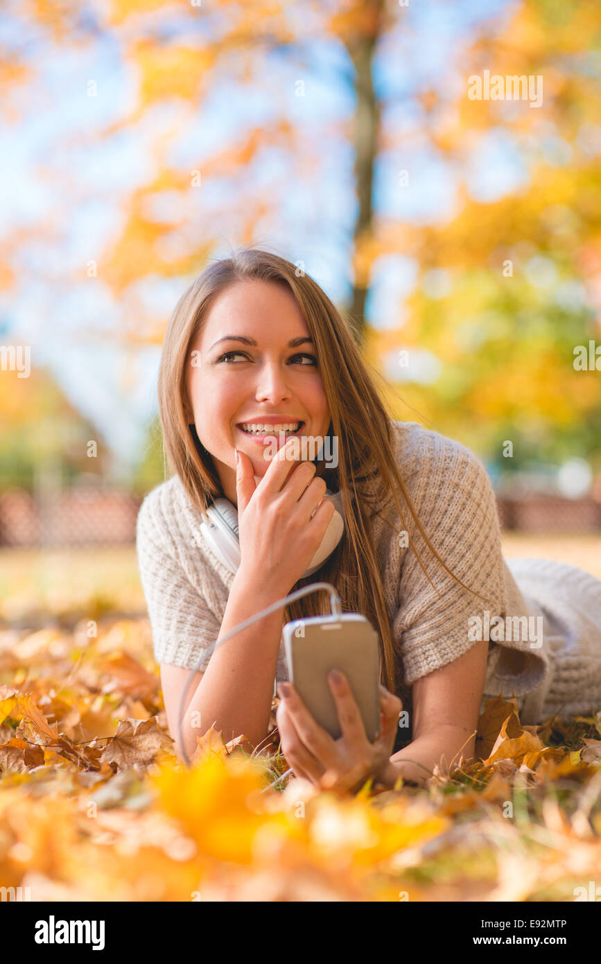 Pretty Smiling Lady Lying on Dry Leaves at Grassy Ground with Mobile ...