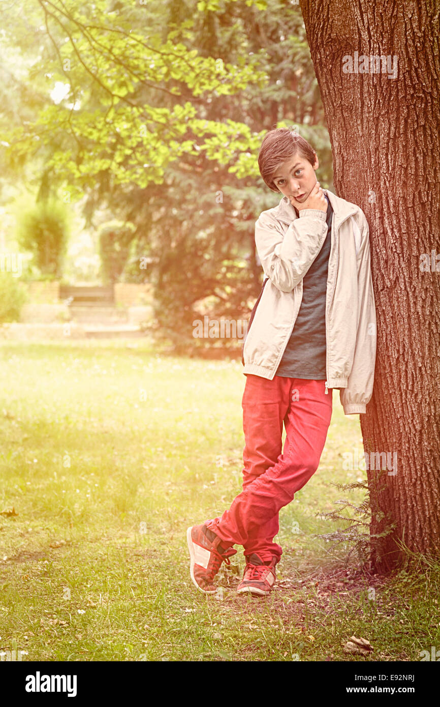 teenage boy leaning against a tree in a park Stock Photo - Alamy