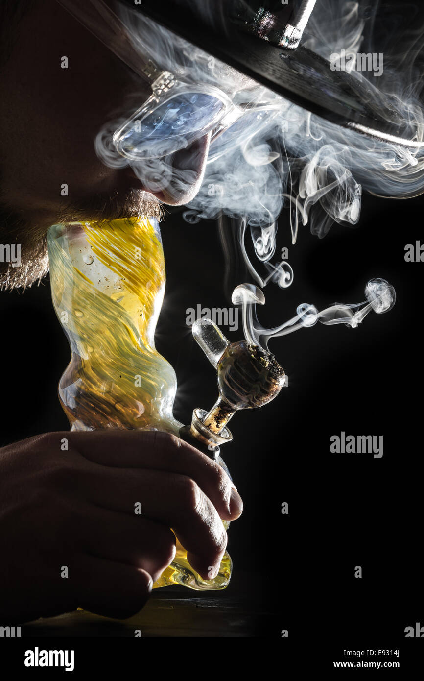 studio shoot with model simulating smoking pot through a bong in a dark ...