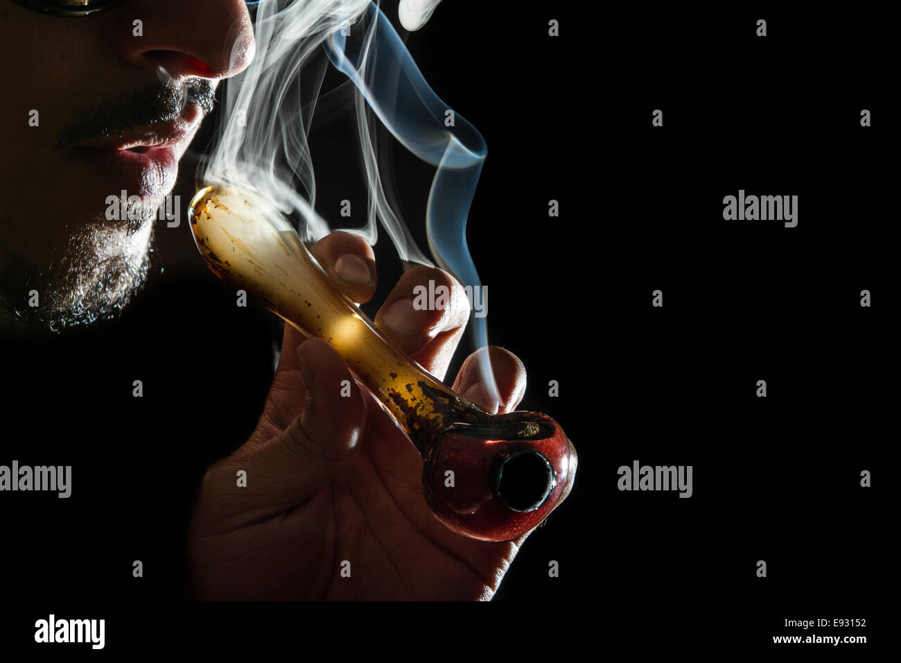 studio shoot with model simulating smoking pot with a pipe in a dark ...
